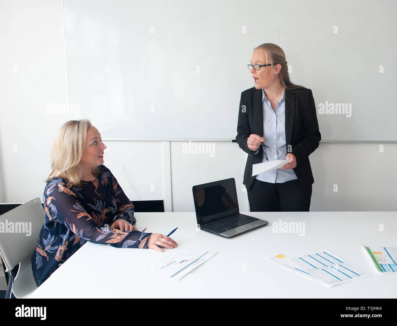 Woman in business suit standing at head of table giving presentation or ...