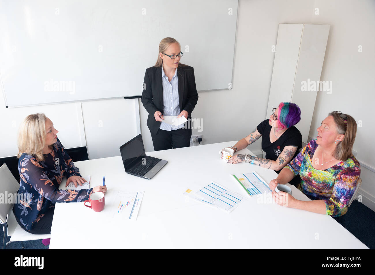 Woman in business suit standing at head of table giving presentation or ...