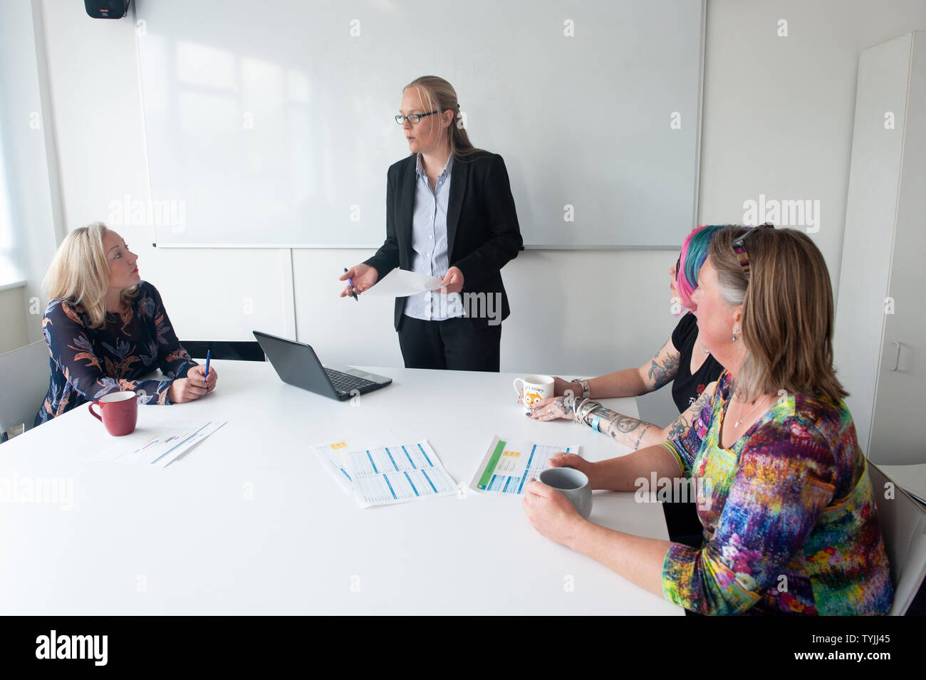 Woman in business suit standing at head of table giving presentation or ...