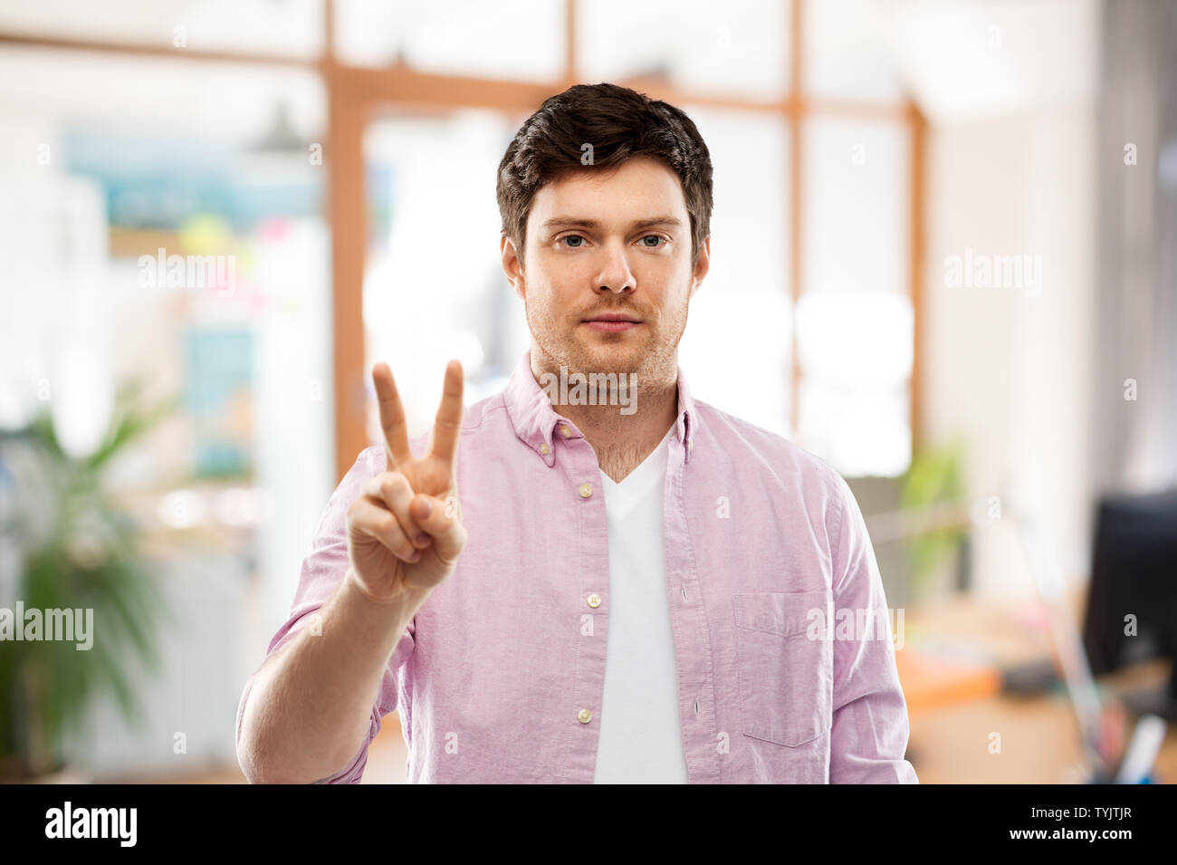young man showing two fingers over office Stock Photo - Alamy