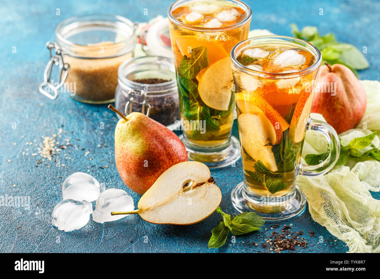 Ice tea with mint leaves and pear in glass cups on a blue background ...