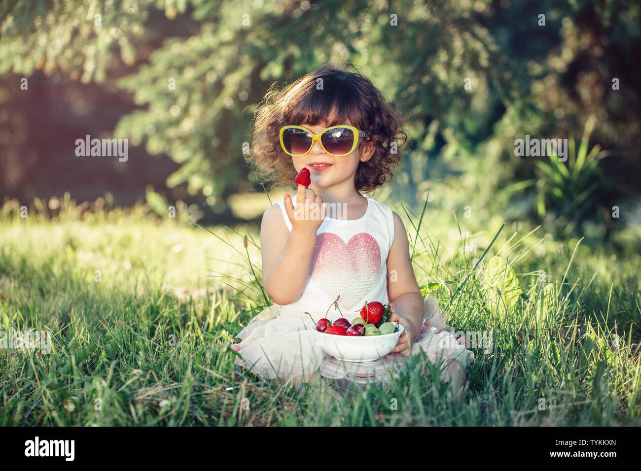 Cute Caucasian toddler baby girl sitting on grass and eating berry ...