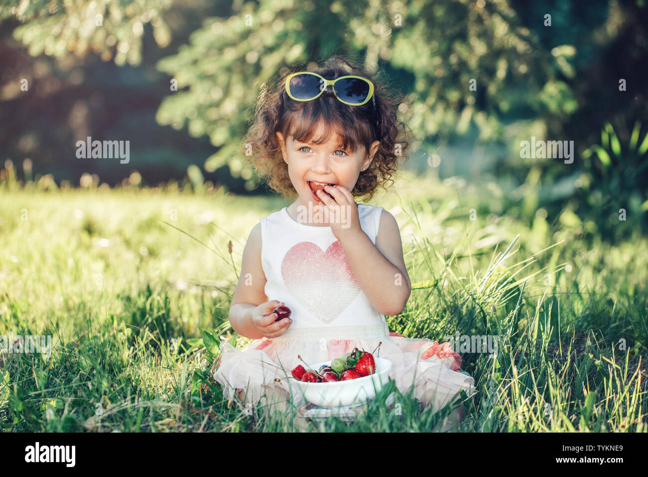 Cute adorable Caucasian toddler baby girl sitting on grass and eating ...
