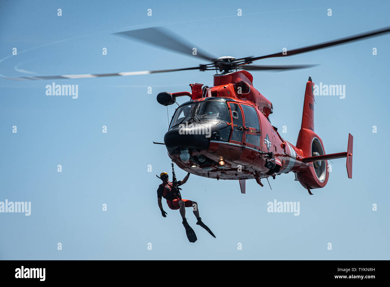 A U.S. Coast Guard (USCG) rescue swimmer hangs of the side of an MH-65 ...