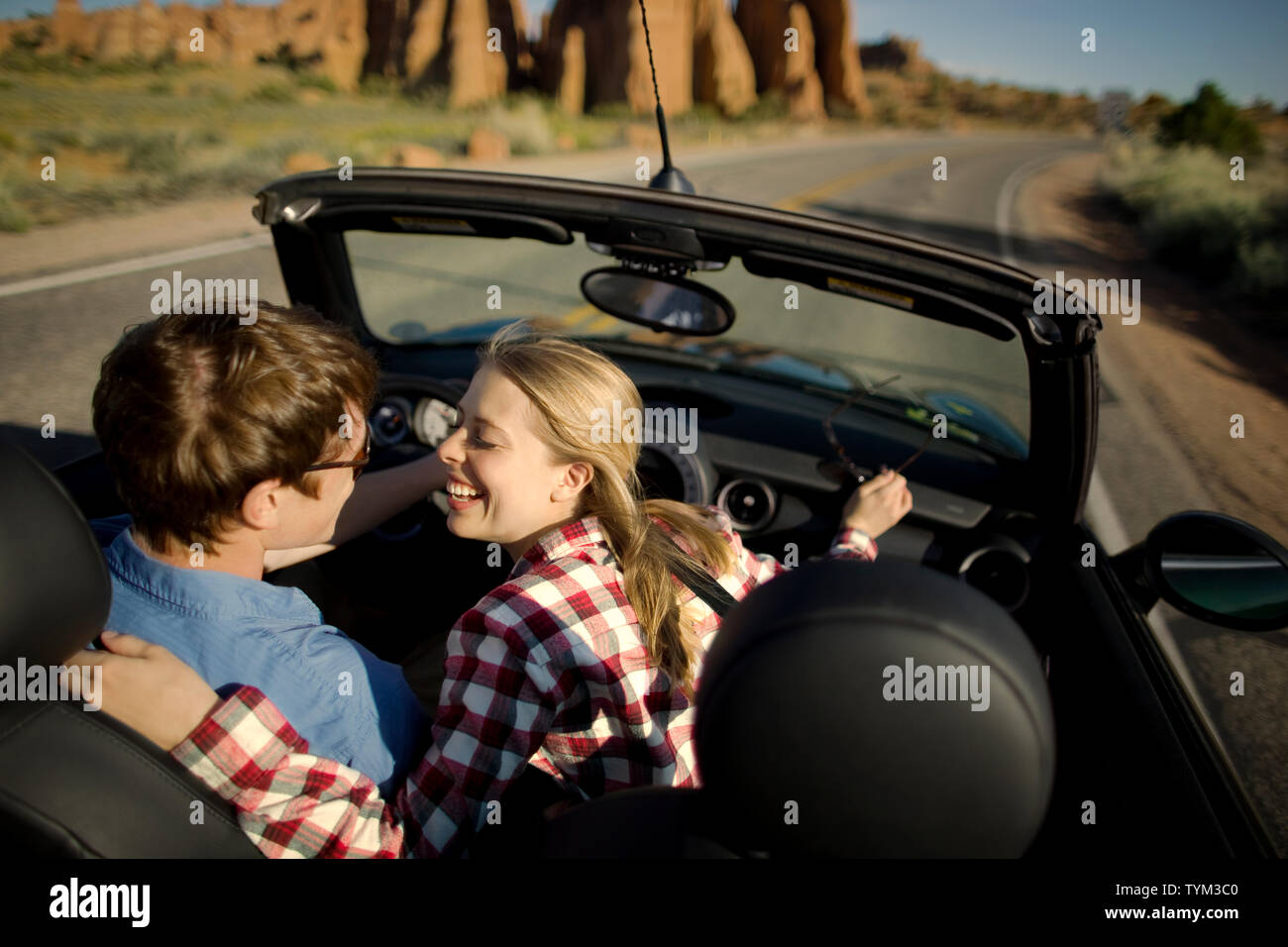 Happy young couple having fun in a convertible car while on a road trip ...