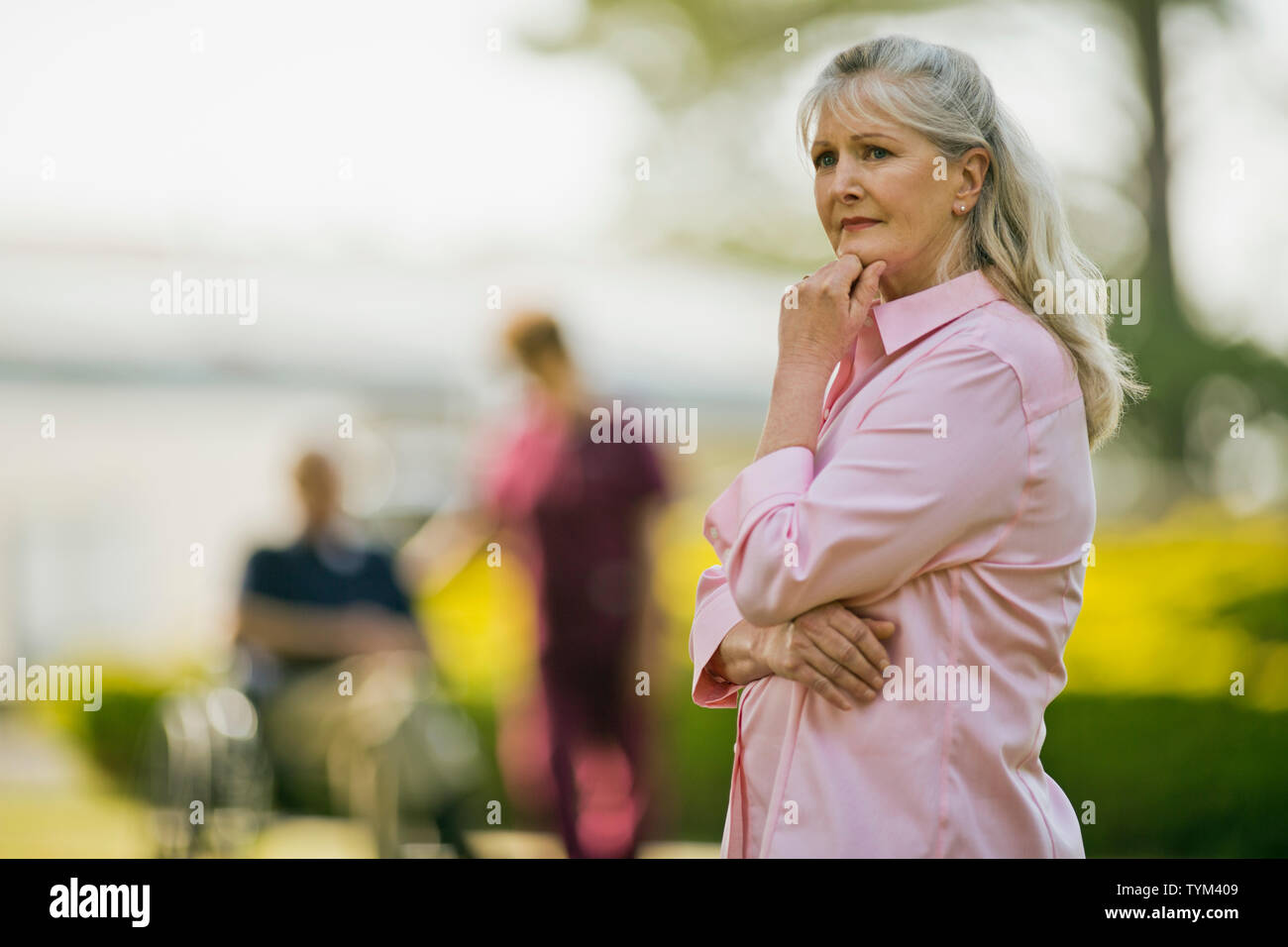 Concerned senior woman standing with her hand on her chin Stock Photo ...