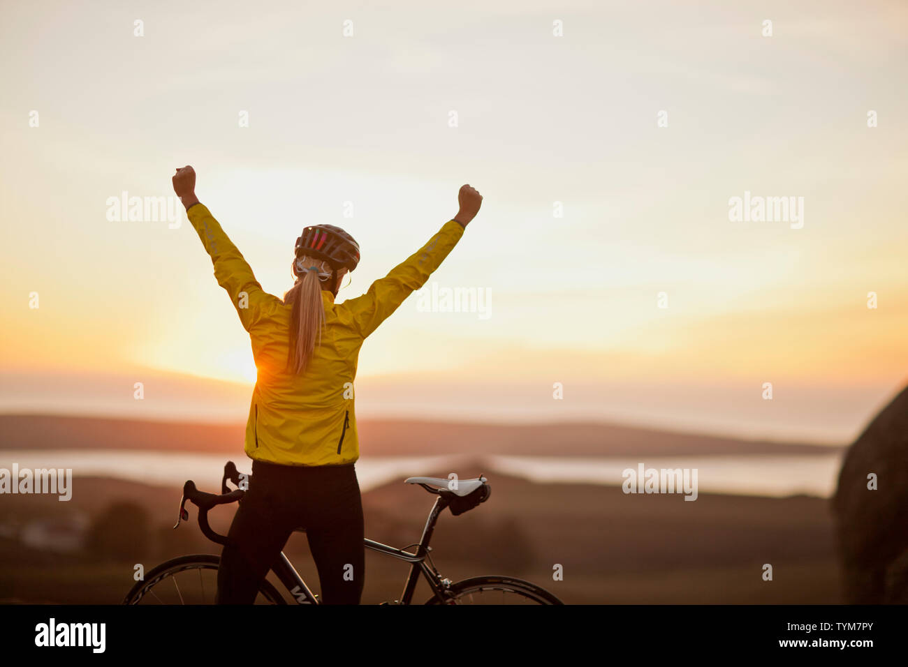 Young woman raising her arms in victory after cycling to the top of a ...