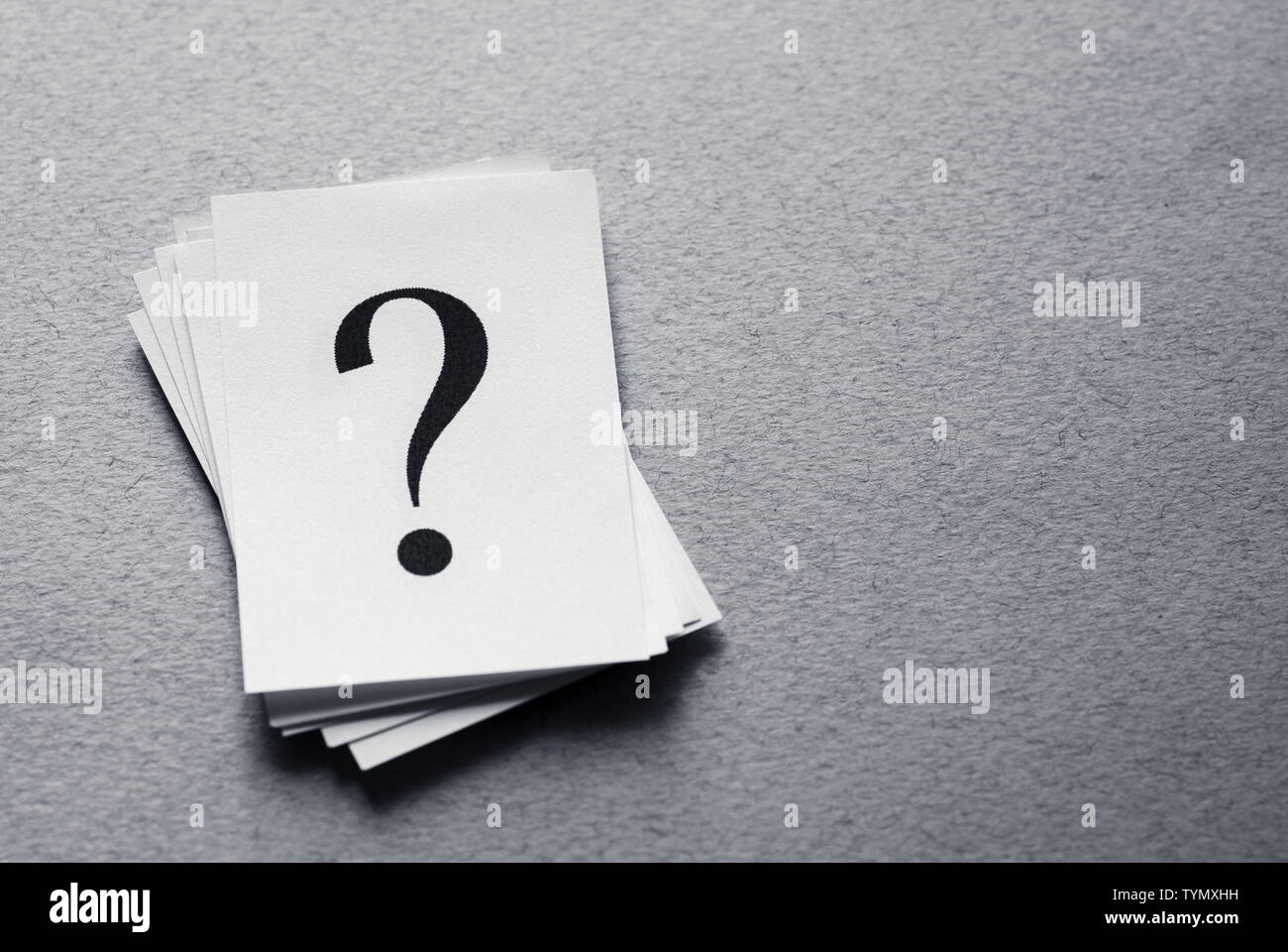 Pile of cards with printed question marks on a textured grey surface ...
