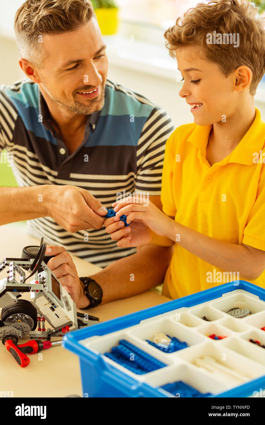 Family cooperation. Joyful nice boy smiling while giving a constructor ...