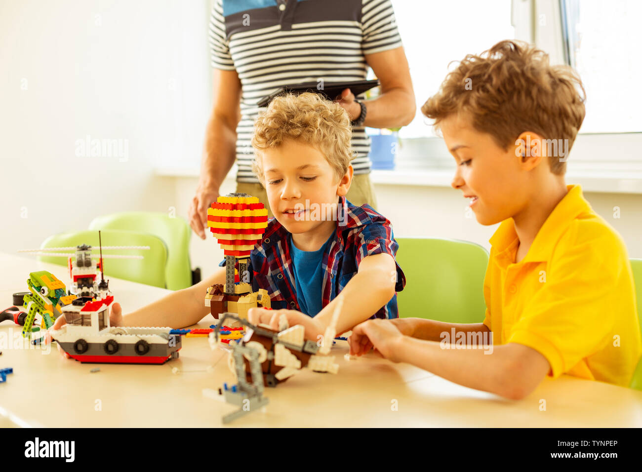 Engaging activity. Happy young boys sitting together at the table while ...