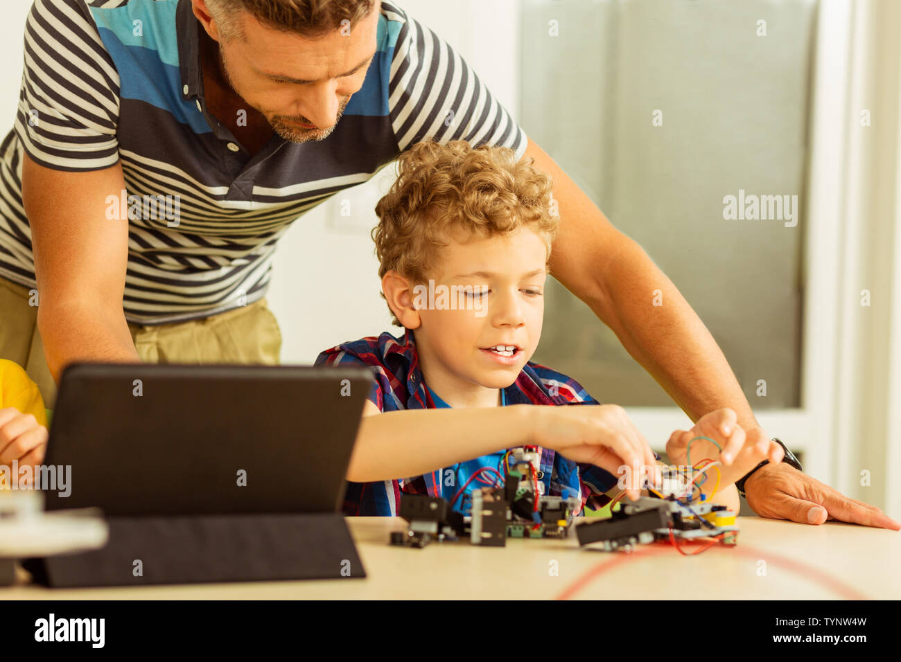 Robotics teacher. Pleasant intelligent man standing behind the boy ...