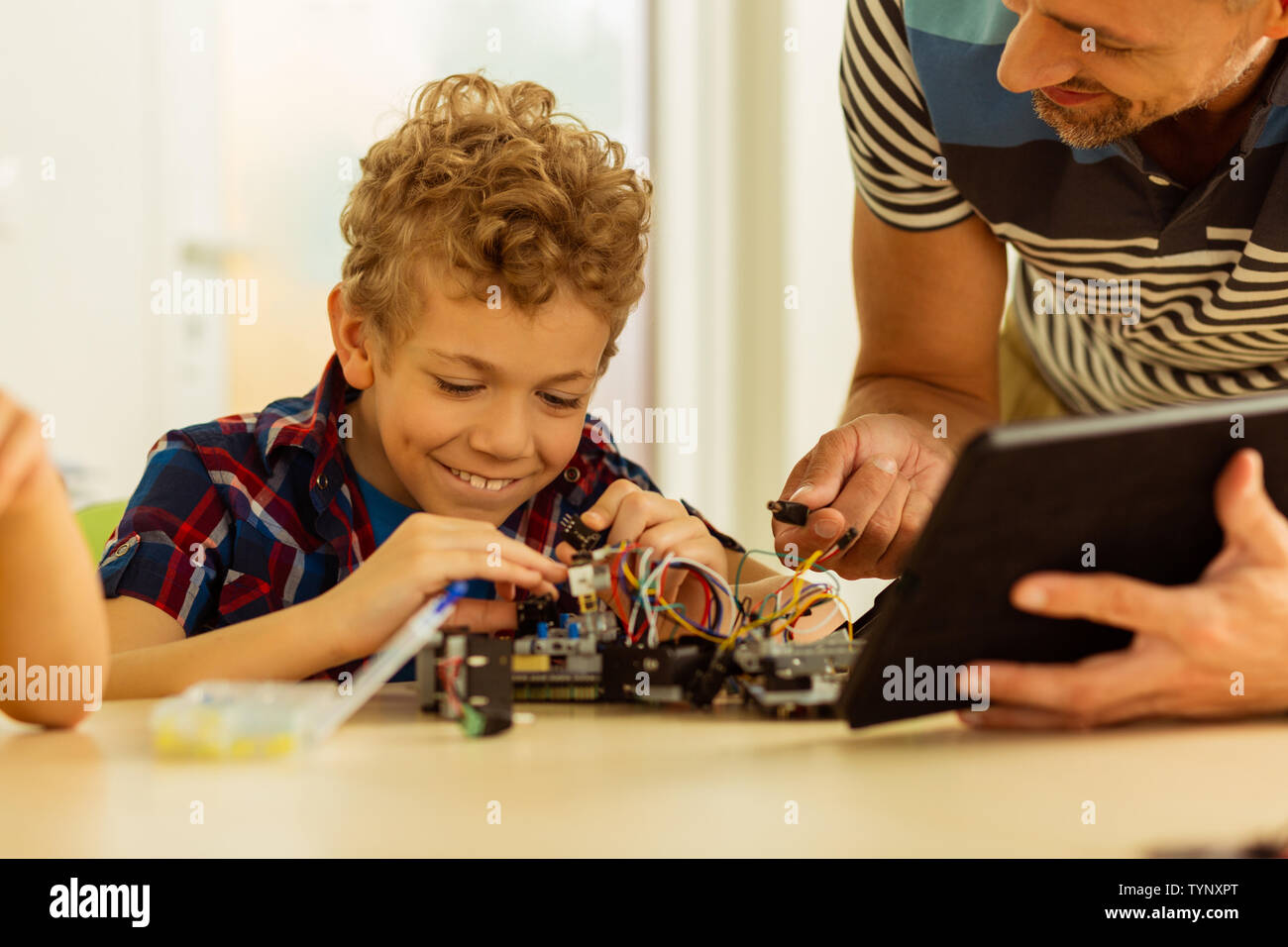 Talented boy. Cheerful happy boy smiling while learning to construct ...