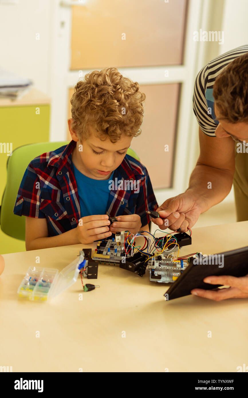 Careful work. Serious cute boy sitting at the table while putting all ...