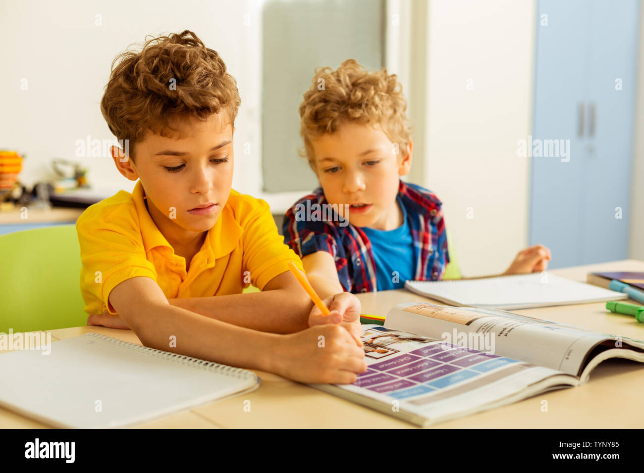 Two classmates. Nice young boys sitting at one desk while having two ...