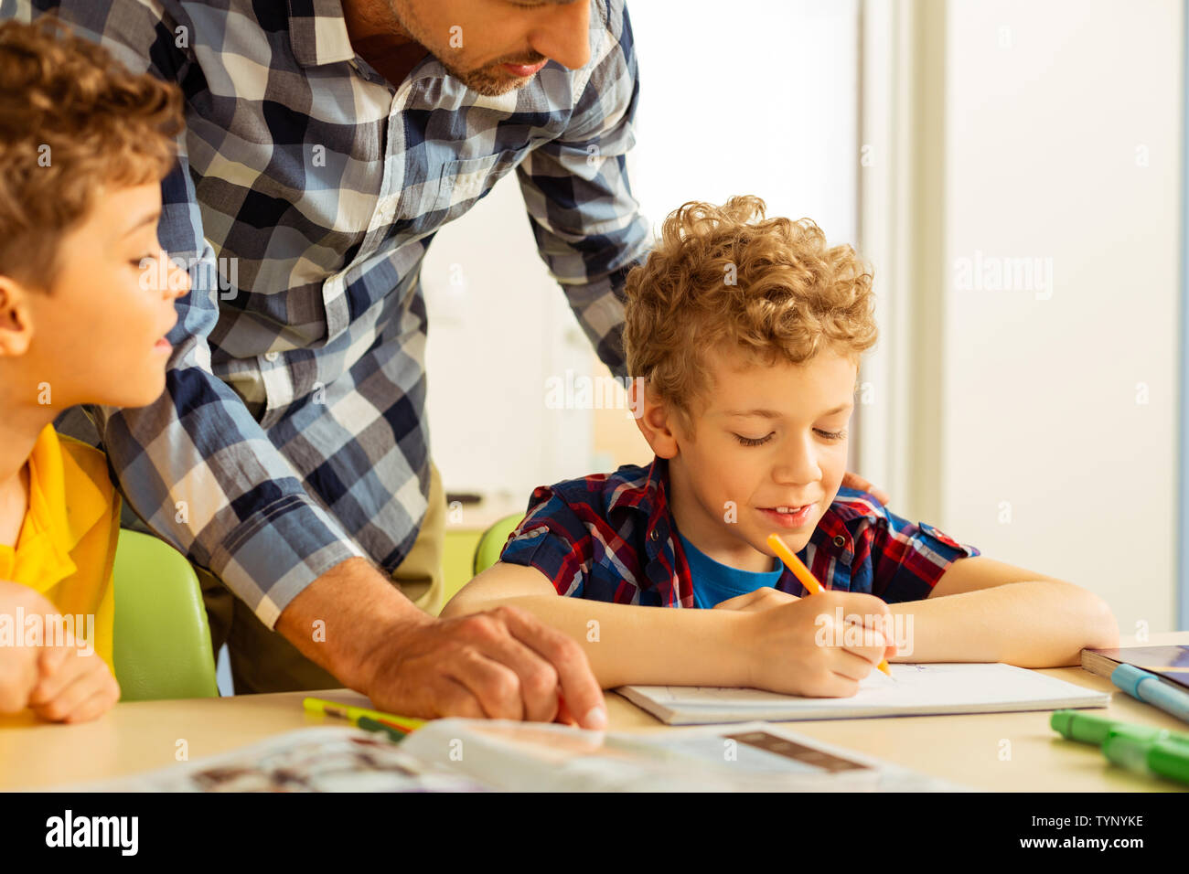 English lesson. Delighted cute boy writing in his notebook while having ...