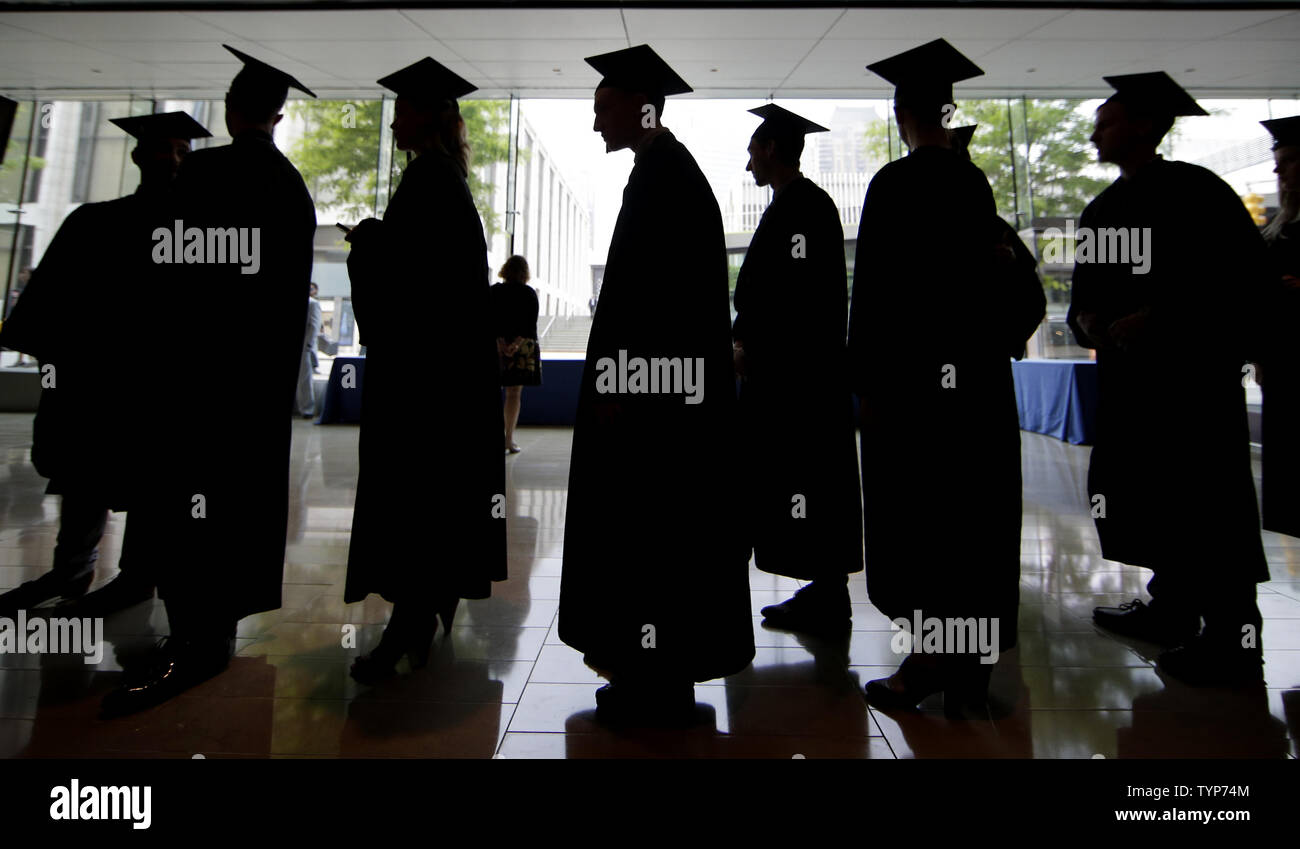 Graduates stand in line wearing caps and gowns before entering the hall ...