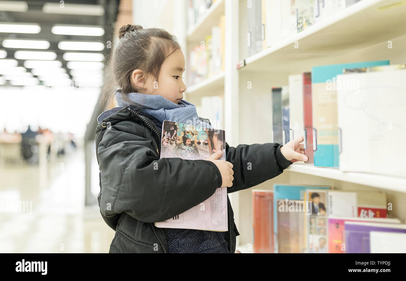 Little Asian girl reading in the library Stock Photo - Alamy