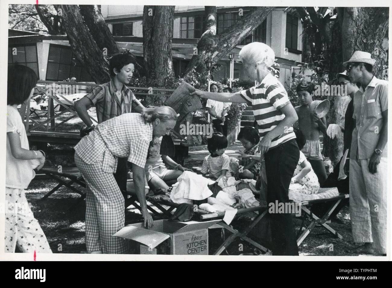 TWO AMERICAN WOMEN HANDING OUT PIECES OF CLOTHING OUT OF A BOX TO ...