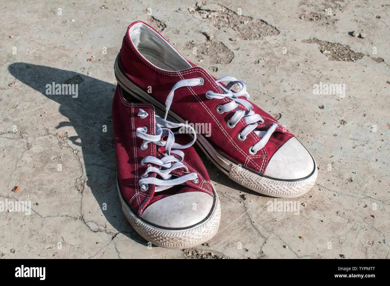 Pair of worn out vintage red old canvas sneakers on outside concrete ...
