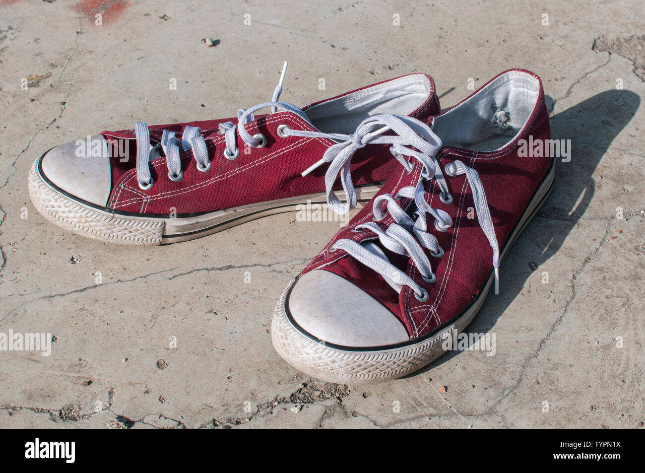 Pair of worn out vintage red old canvas sneakers on outside concrete ...