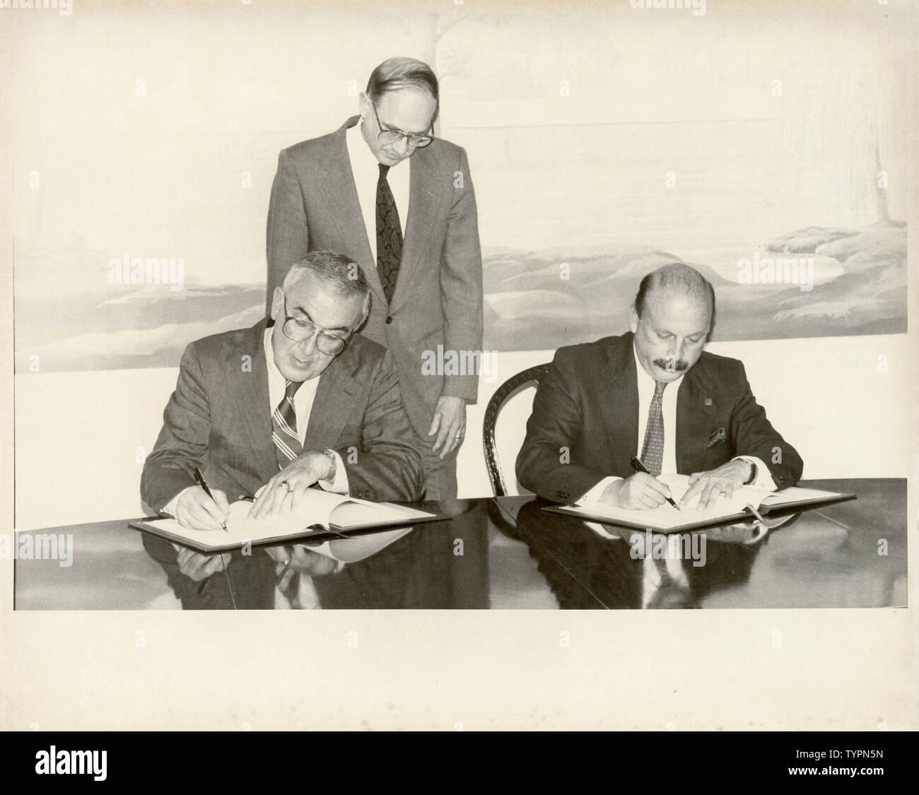GROUP OF MEN SIGNING PAPERS AT TABLE. MEN STANDING UP OBSERVING Stock ...