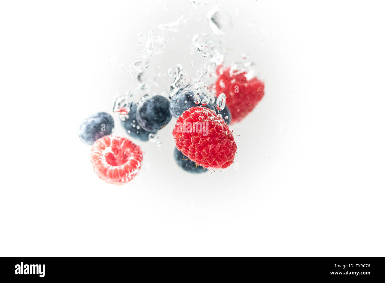 Blueberry’s and raspberries splashing into crystal clear water with air ...