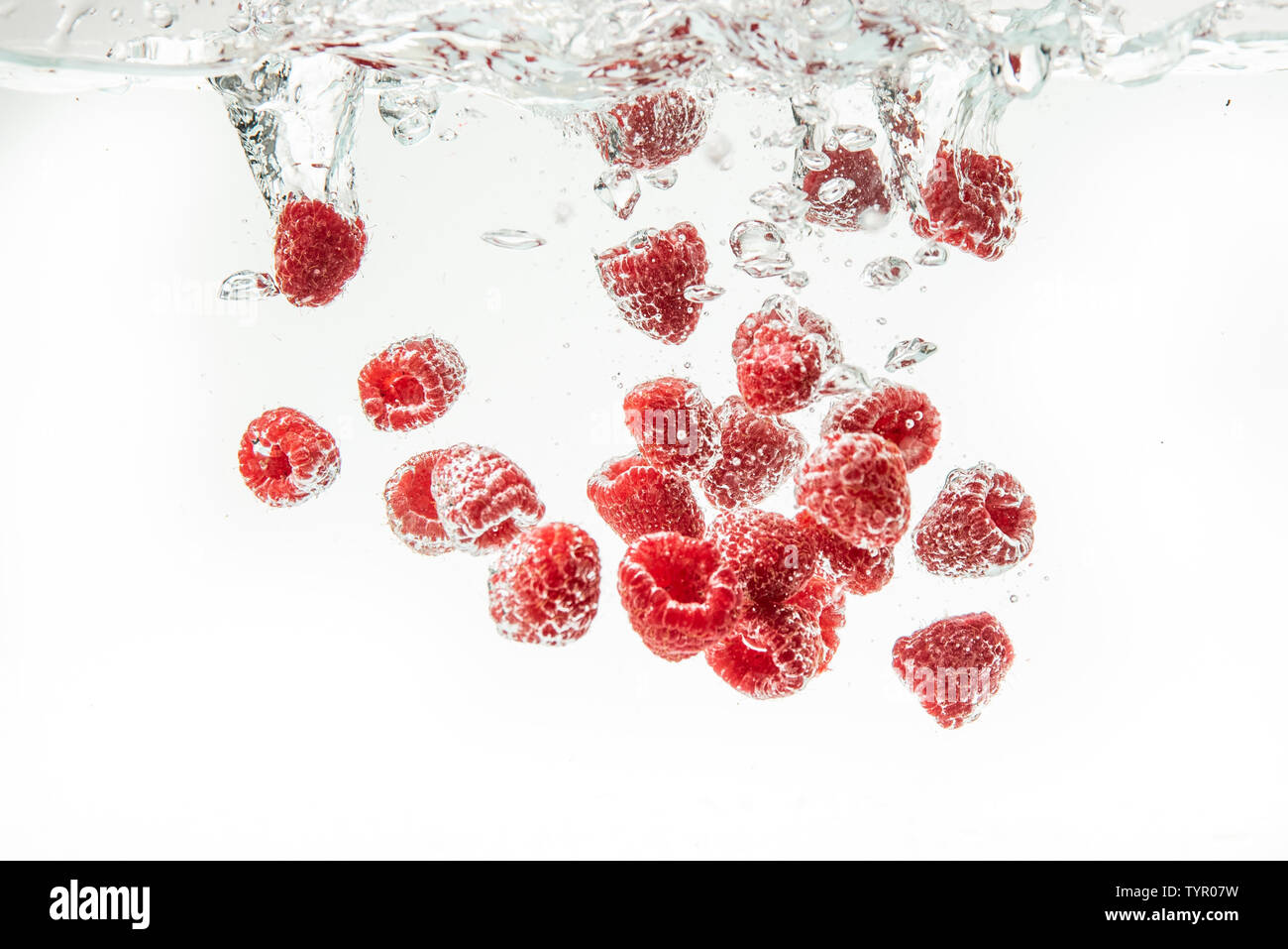 Bunch of Raspberries splashing into crystal clear water with air ...