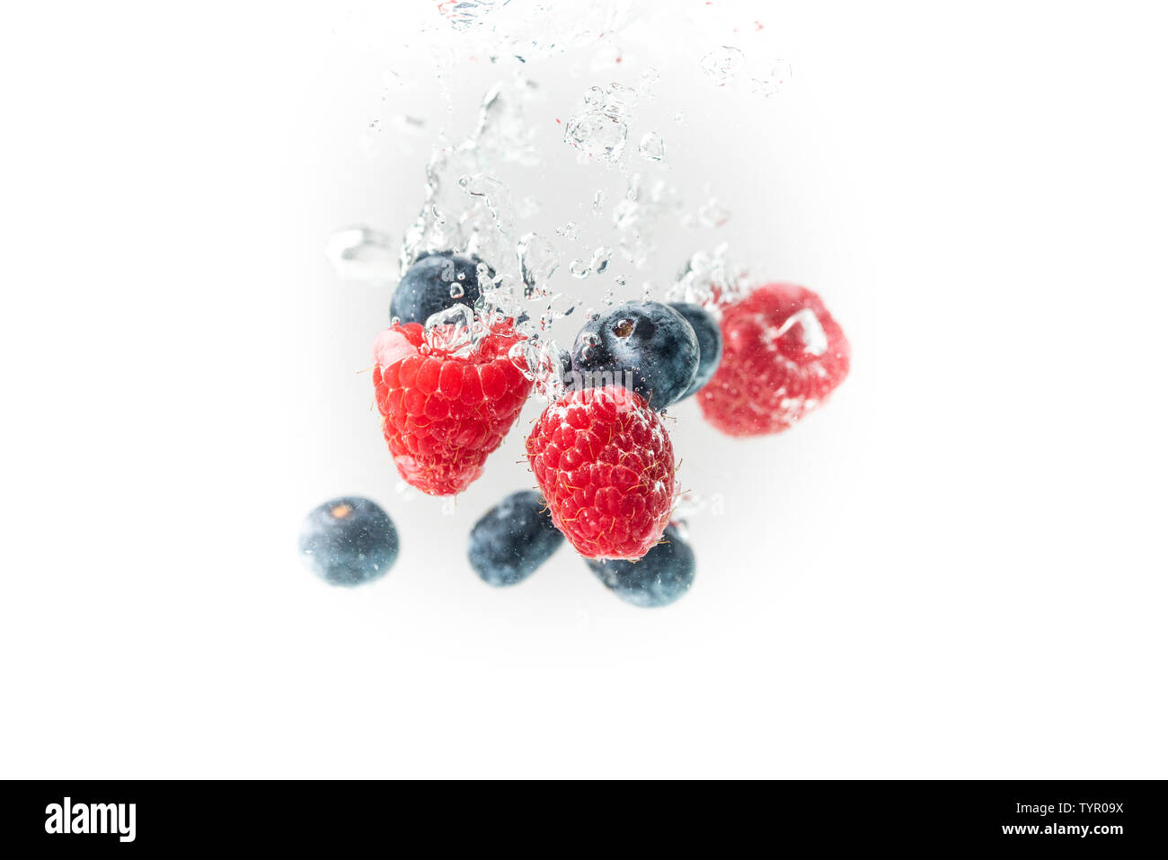 Blueberry’s and raspberries splashing into crystal clear water with air ...