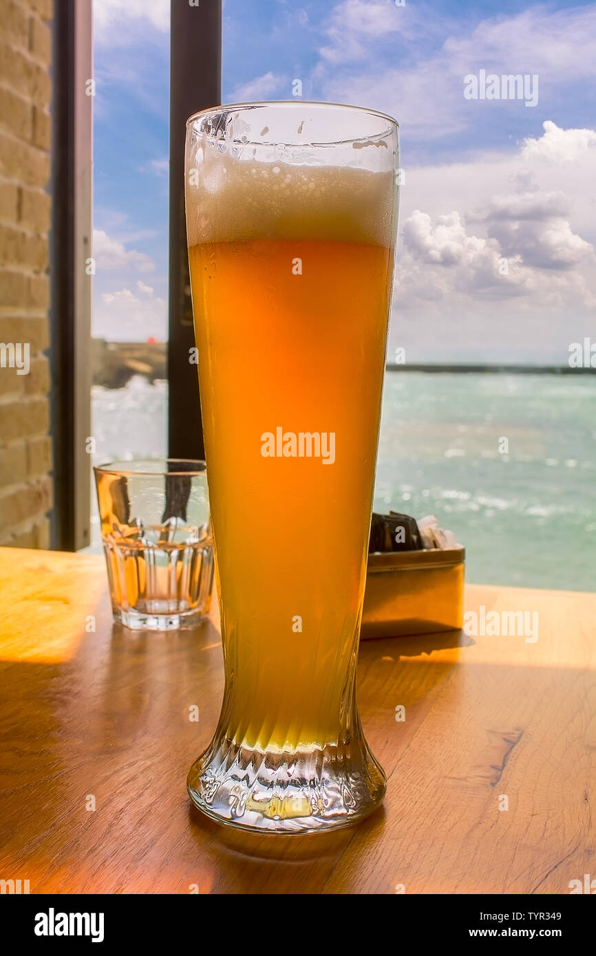 A glass of cold sweaty beer on a table in a bar overlooking the sea ...
