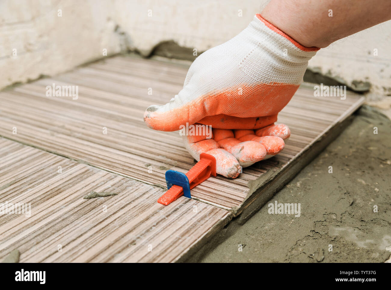 Tiler's hand is using plastic wedges and clips for aligning tiles ...