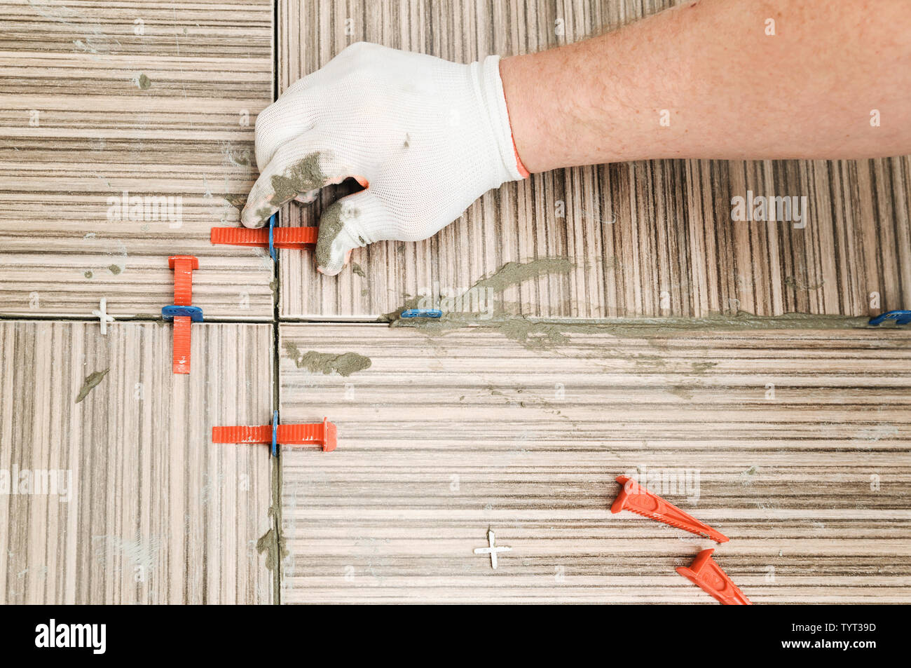 Tiler's hand is using plastic wedges and clips for aligning tiles ...