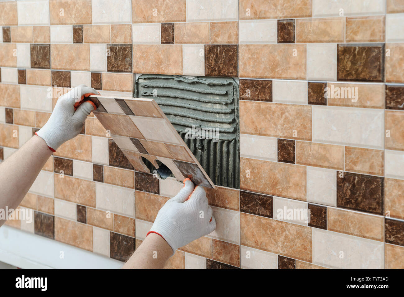 The tiler's hands are installing a tile with holes for electric boxes ...