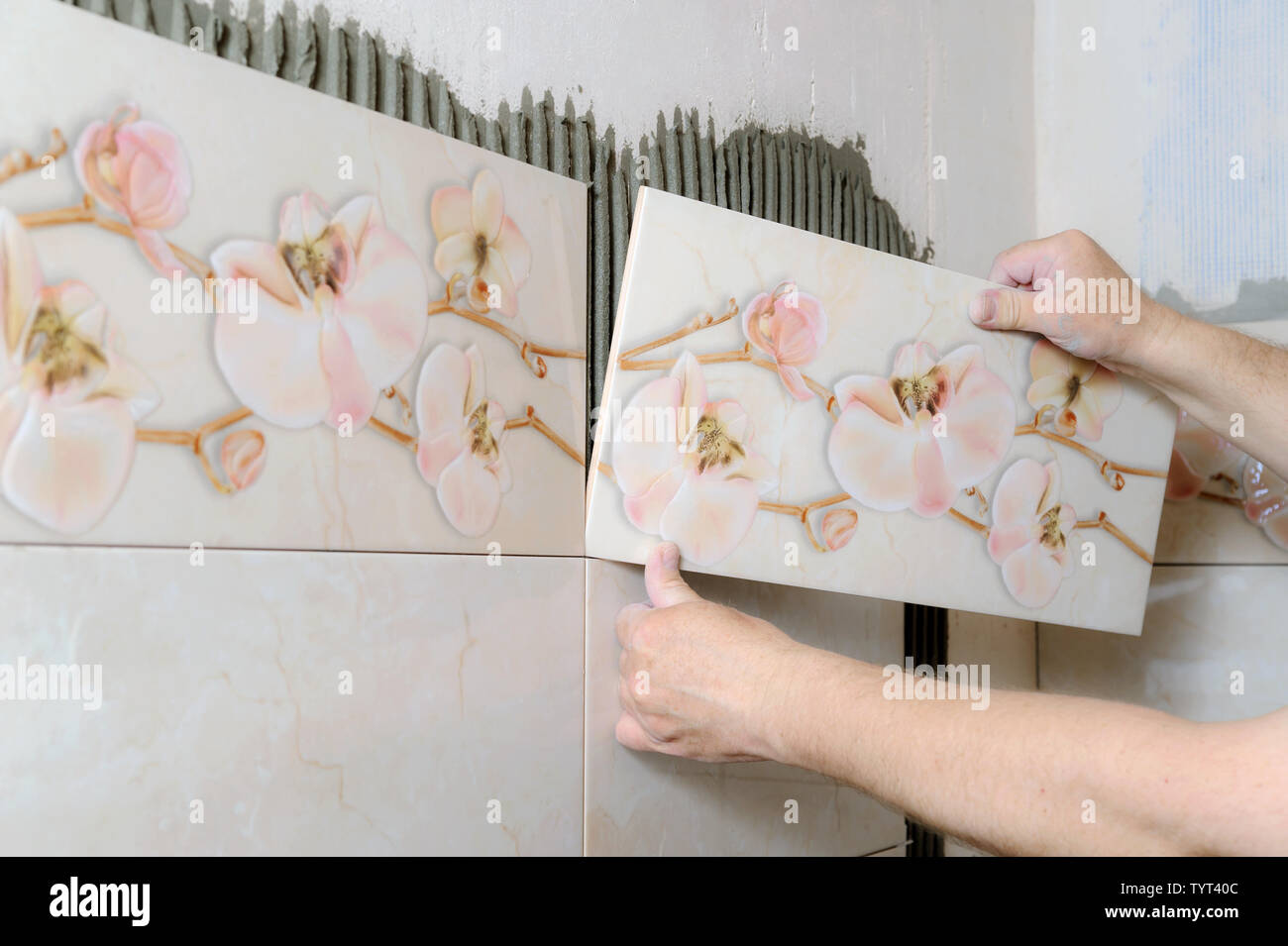 Tilers hands are installing a ceramic tile on a wall in a bathroom ...