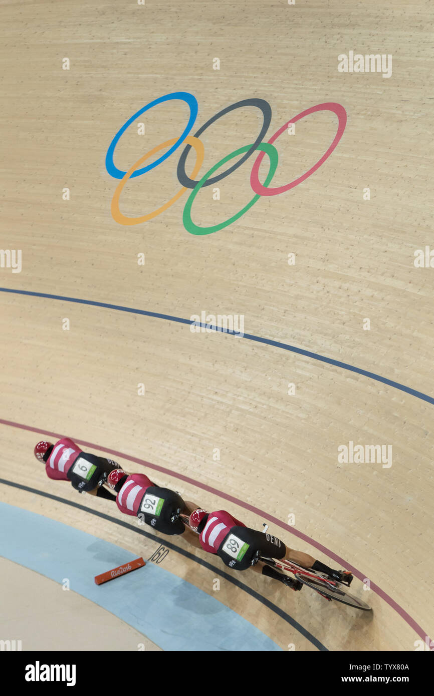 Cyclists from the Denmark team speed past the Olympic ring symbol ...