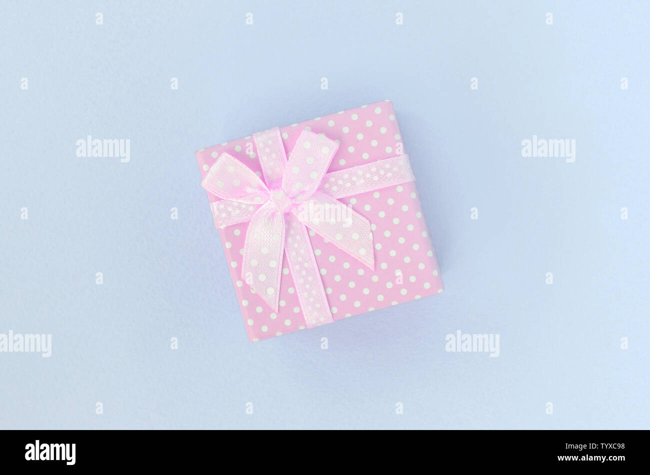 Small pink gift box with ribbon lies on a violet background. Minimalism ...