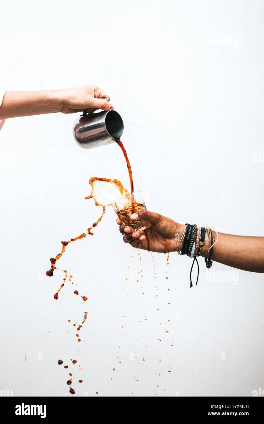 Female's hand pouring and splashing a dark liquid into a glass held by ...
