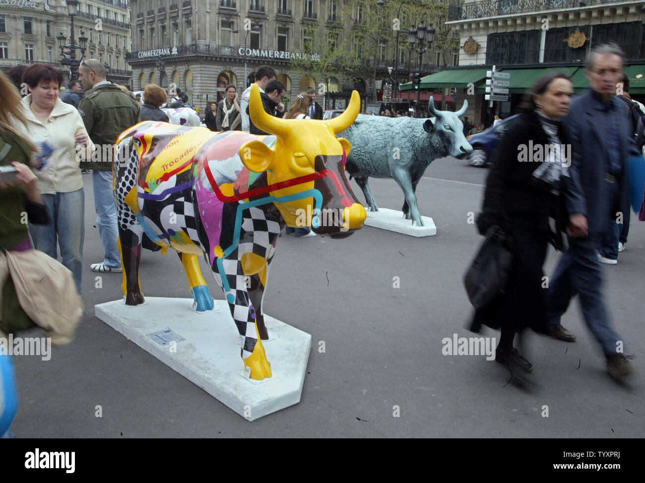 Pedestrians stroll past statues of cows set up on the pavement at the ...