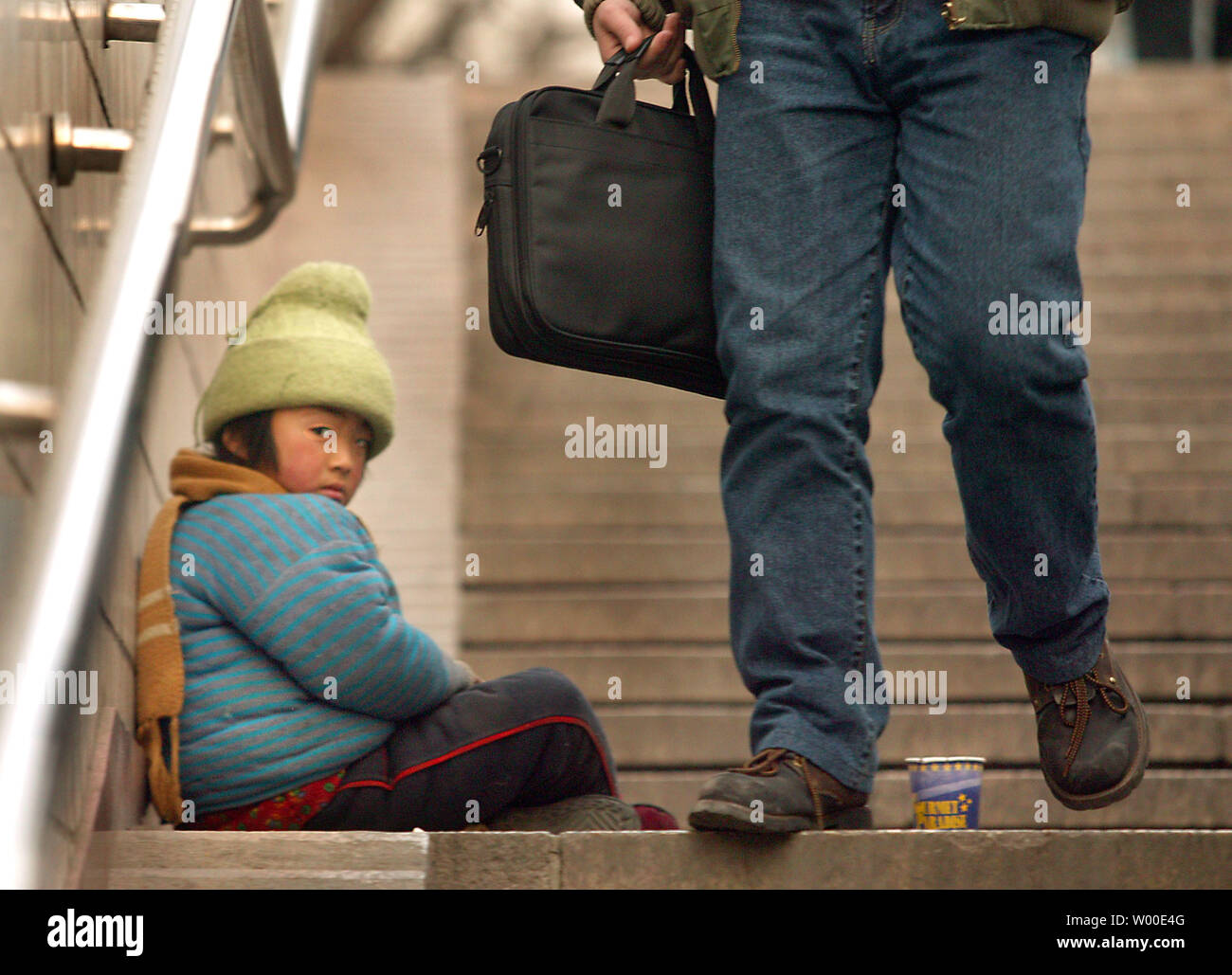 A young Chinese boy begging for money sits on the steps leading down to ...