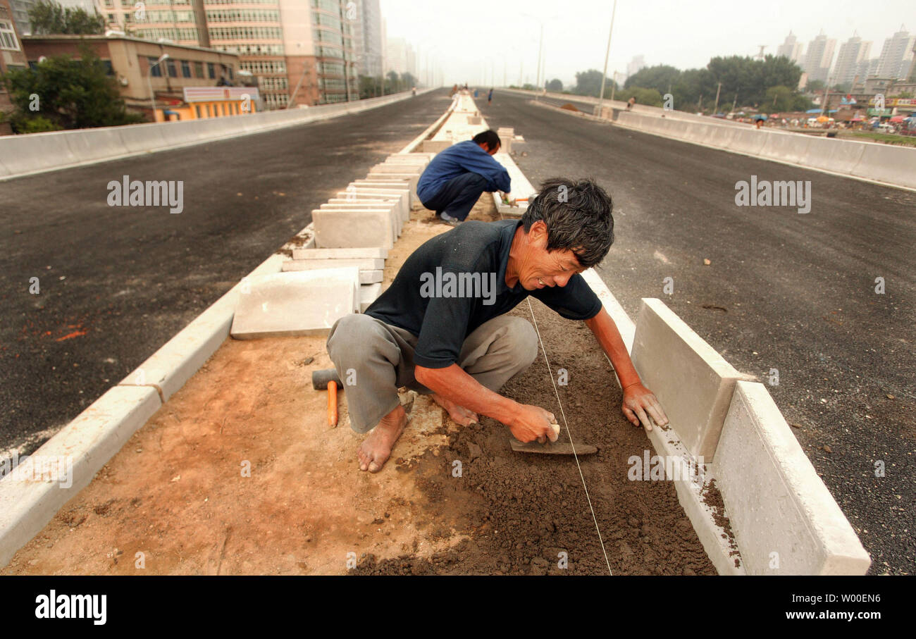 A Chinese man prepares to lay concrete bricks into place in the middle ...
