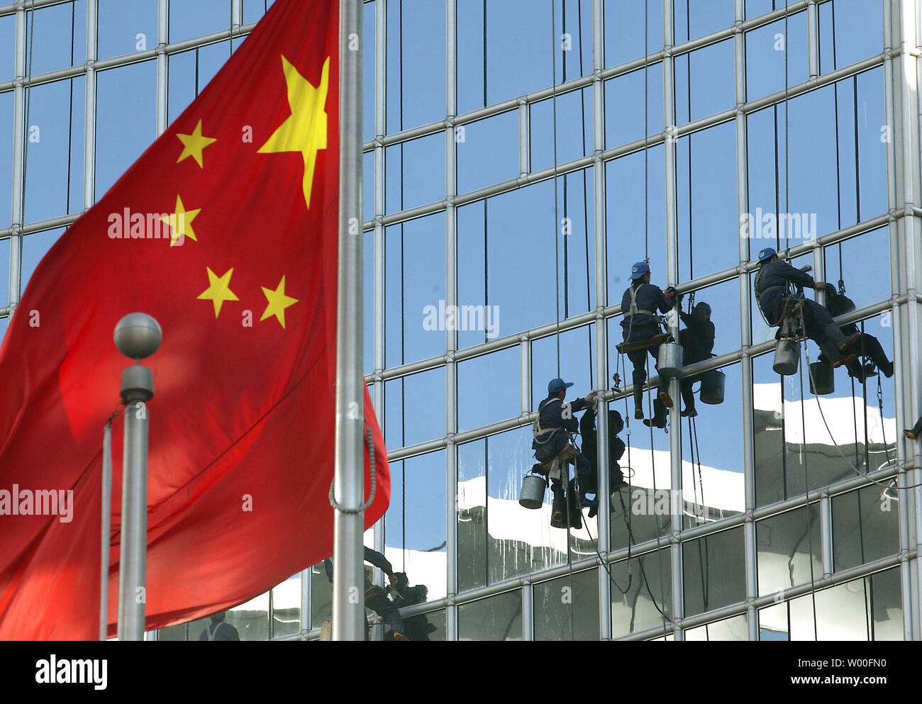 Chinese window cleaners sit on wooden boards attached to ropes as they ...