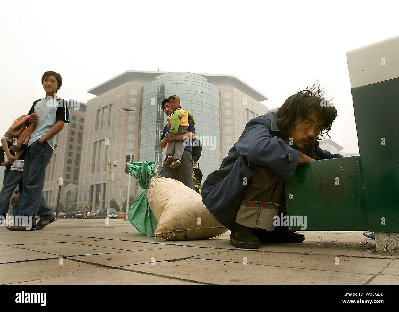 A homeless Chinese man looks for bits of food in a trash bin outside a ...