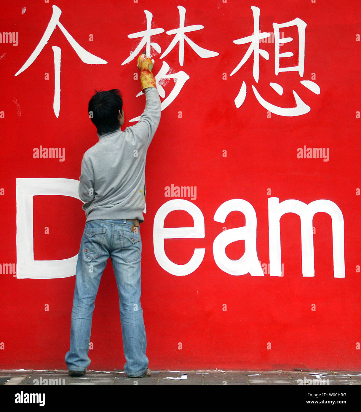 A Chinese artist paints Olympic logos and icons on a long concrete wall ...