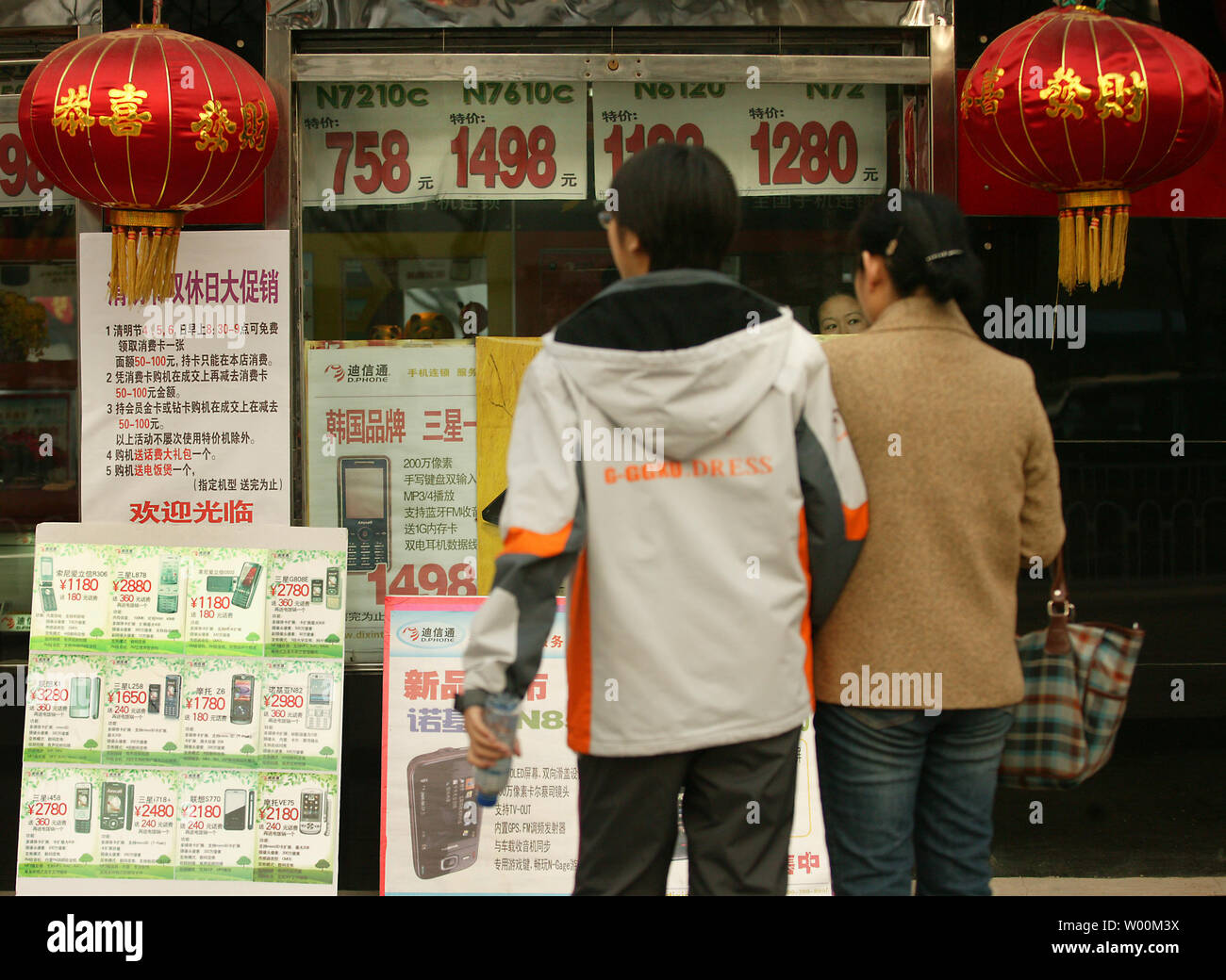 A Chinese couple stops to look at the sale prices of mobile phones ...