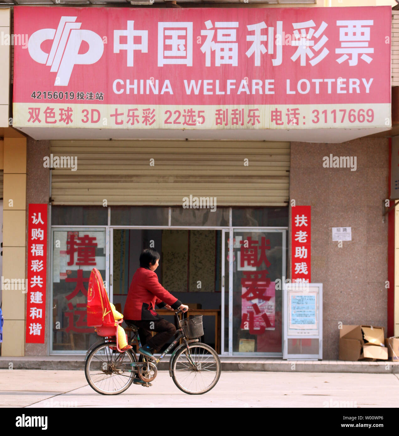 A woman and her child cycle past a China Welfare Lottery office in ...