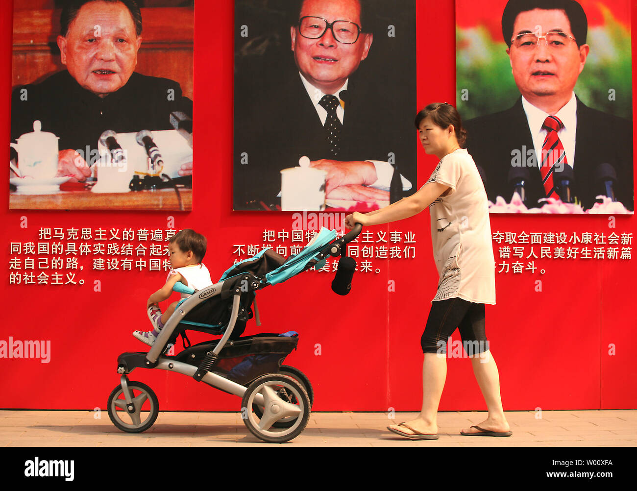 A woman pushes a baby trolly past photos of previous Chinese leaders ...