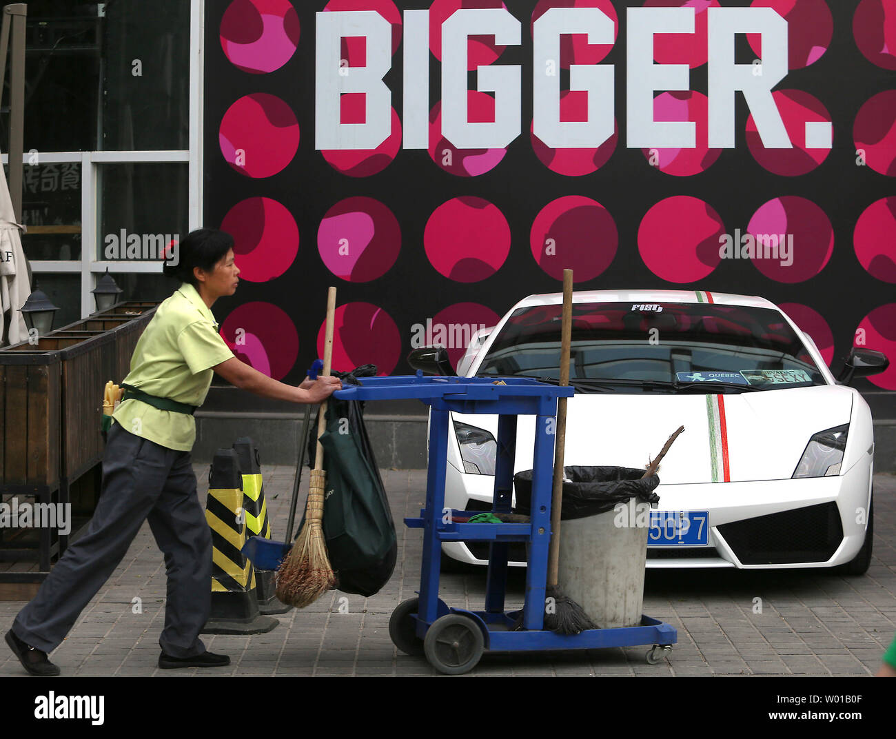 A Chinese custodial worker sweeps the parking lot near a Lamborghini ...
