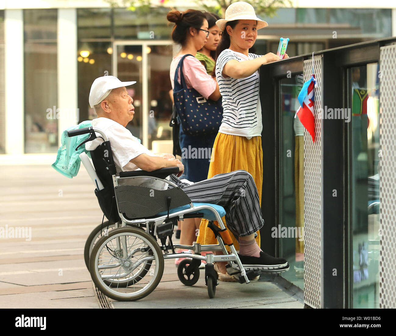 A Chinese senior citizen is escorted by a younger woman through a plaza ...