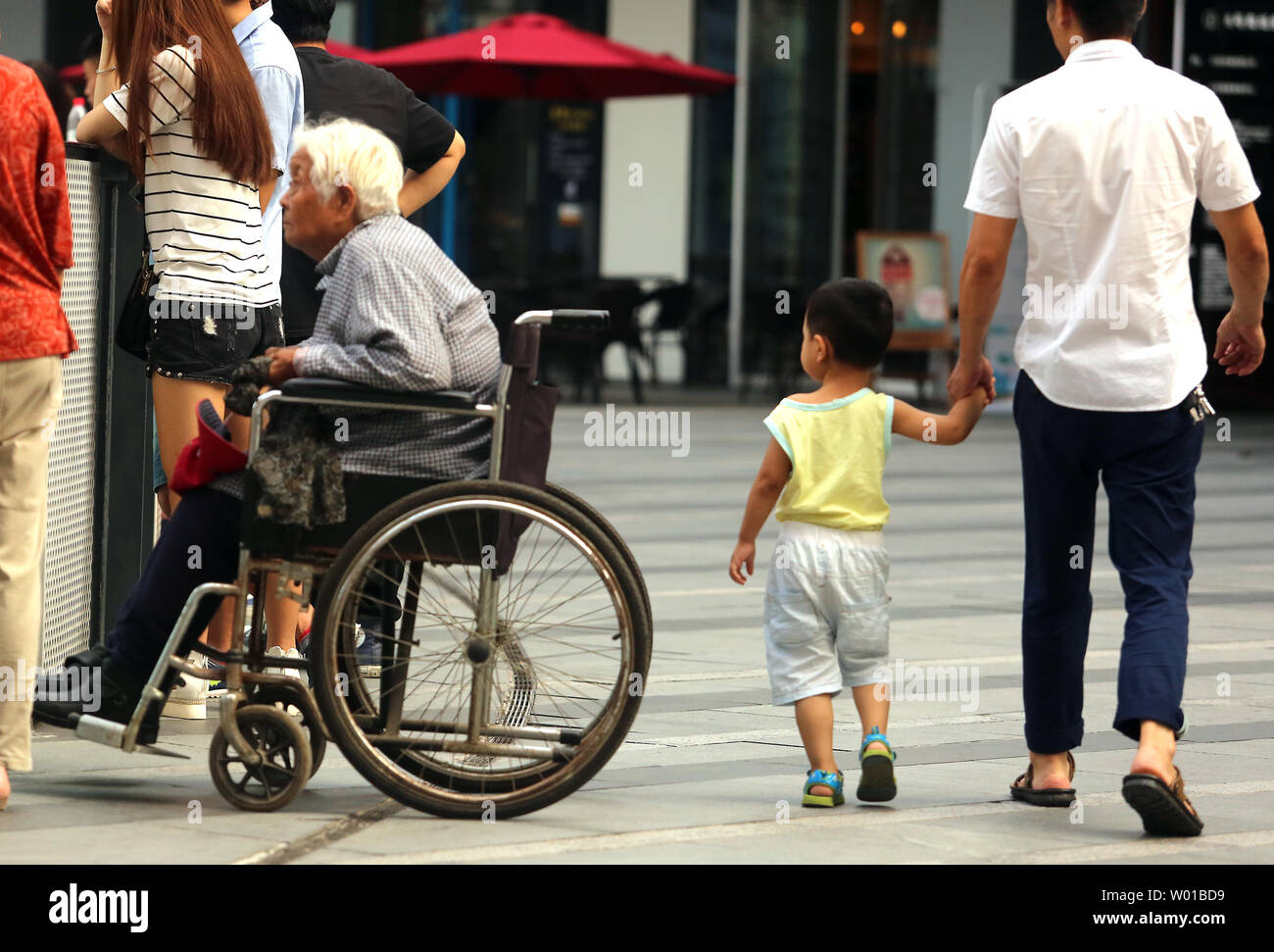 A Chinese senior citizen watches a performance in a plaza on a sunny ...