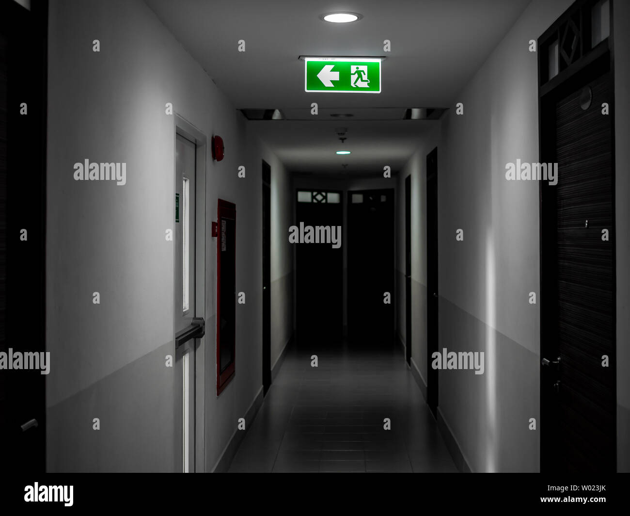 Green exit fire sign hanging on ceiling on dark mysterious corridor in ...