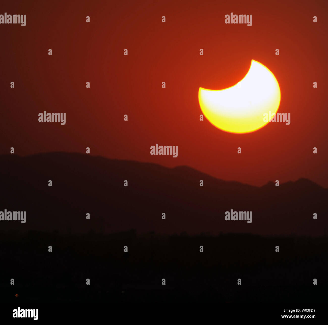 The Sun is partially covered by the Moon as it approaches the horizon ...